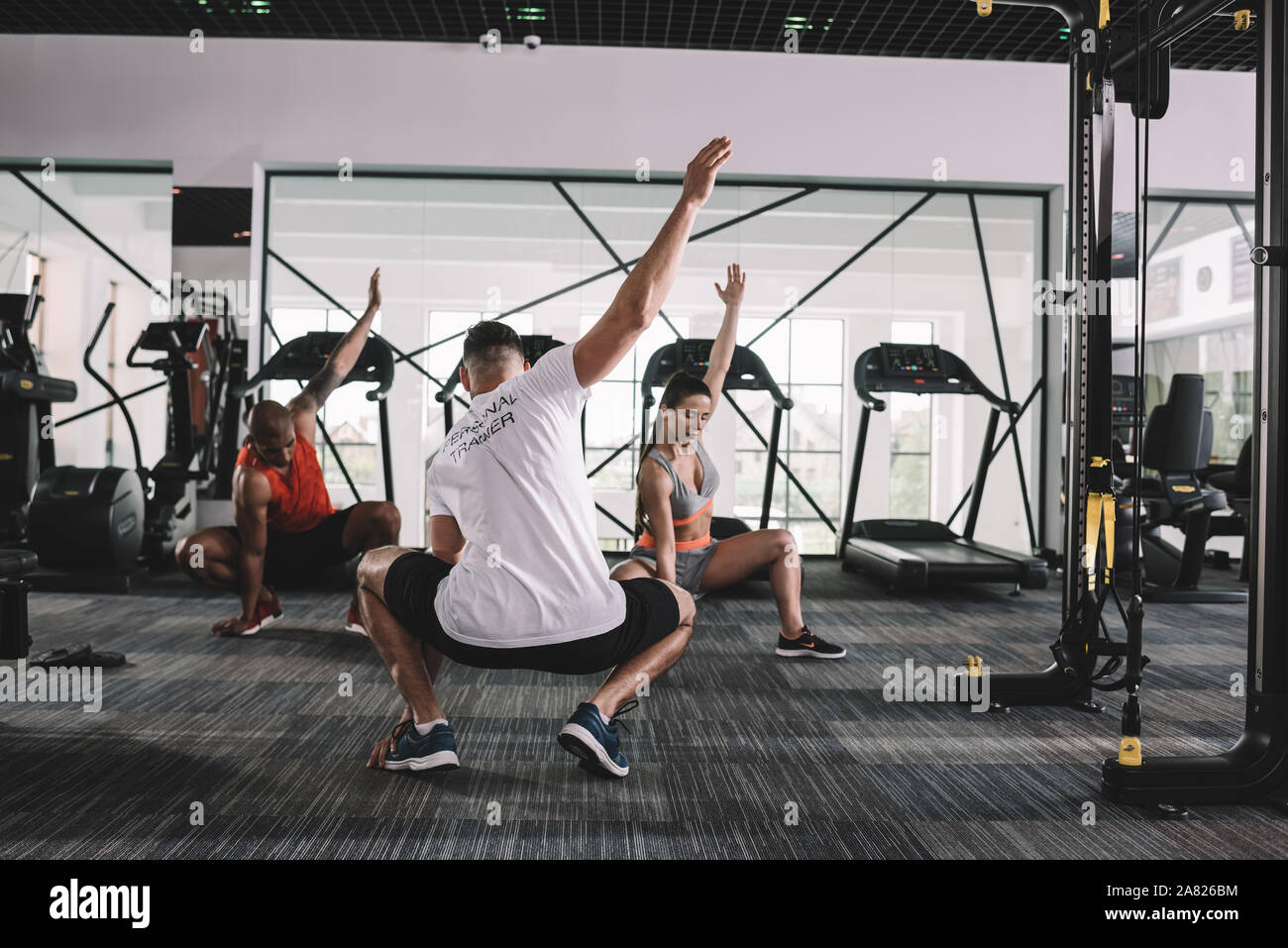 back view of trainer squatting with raised hand together with ...