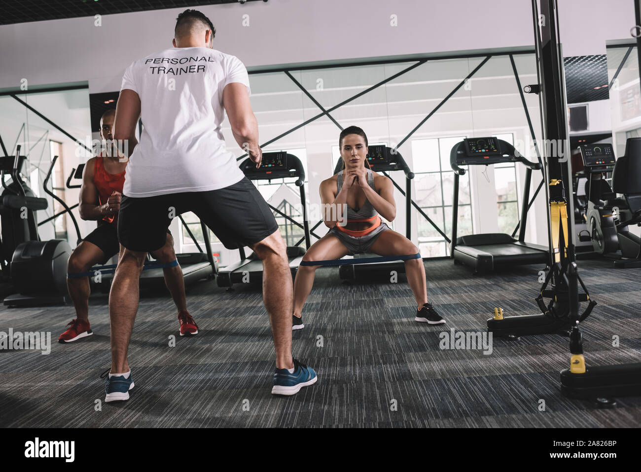 back view of personal trainer standing near multicultural athletes ...