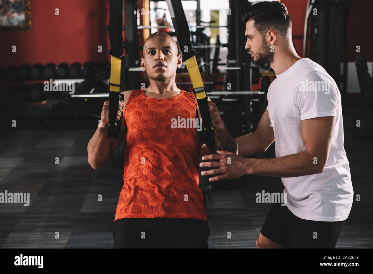 attentive trainer supporting young african american athlete pulling up ...