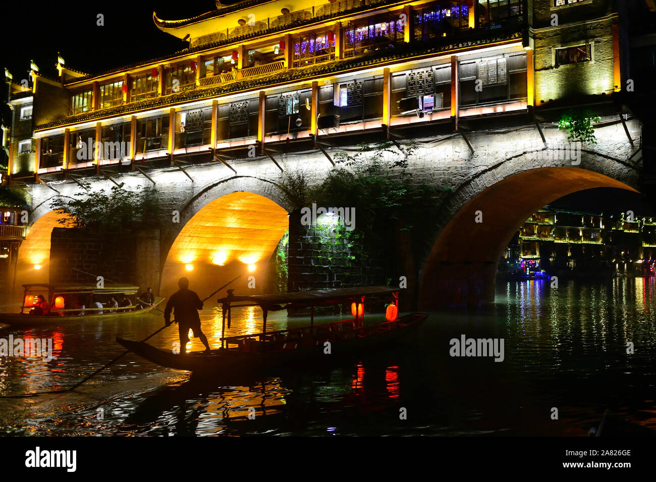 The nighttime silhouette of a man pushing a sampan boat, floats under ...
