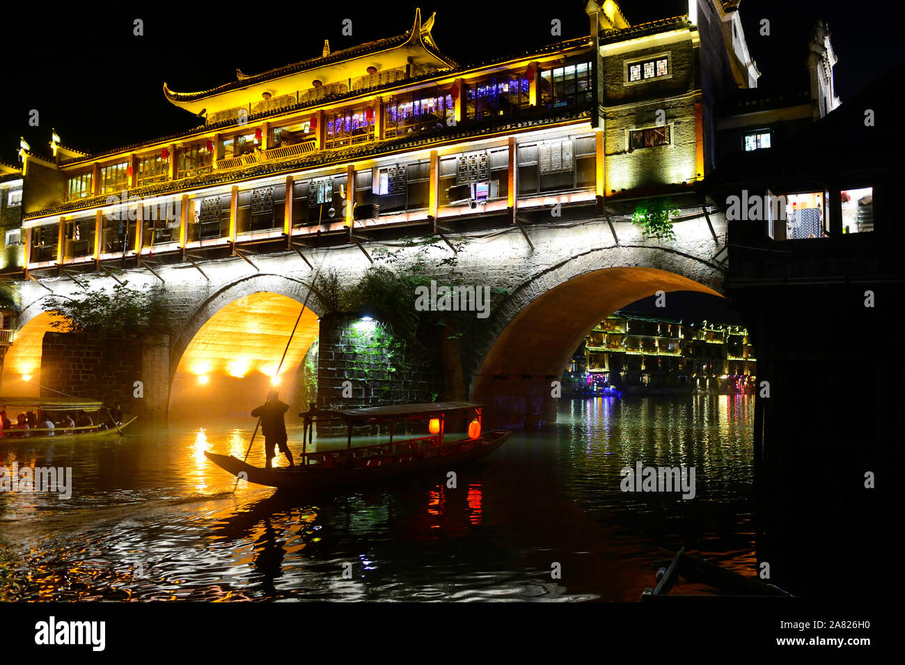 The nighttime silhouette of a man pushing a sampan boat, floats under ...