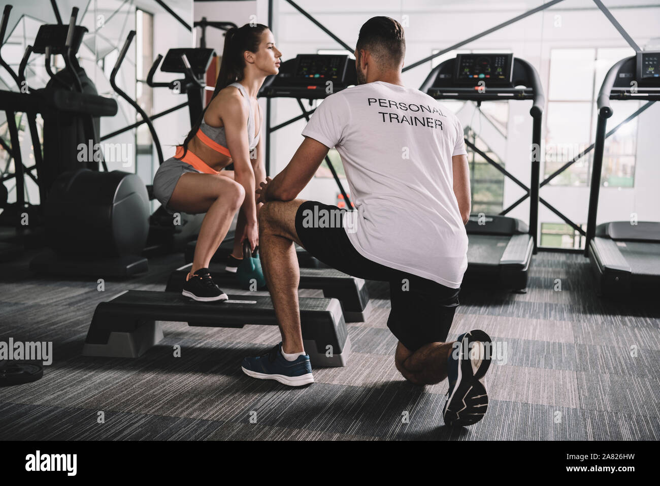 back view of personal trainer instructing young sportswoman lifting ...