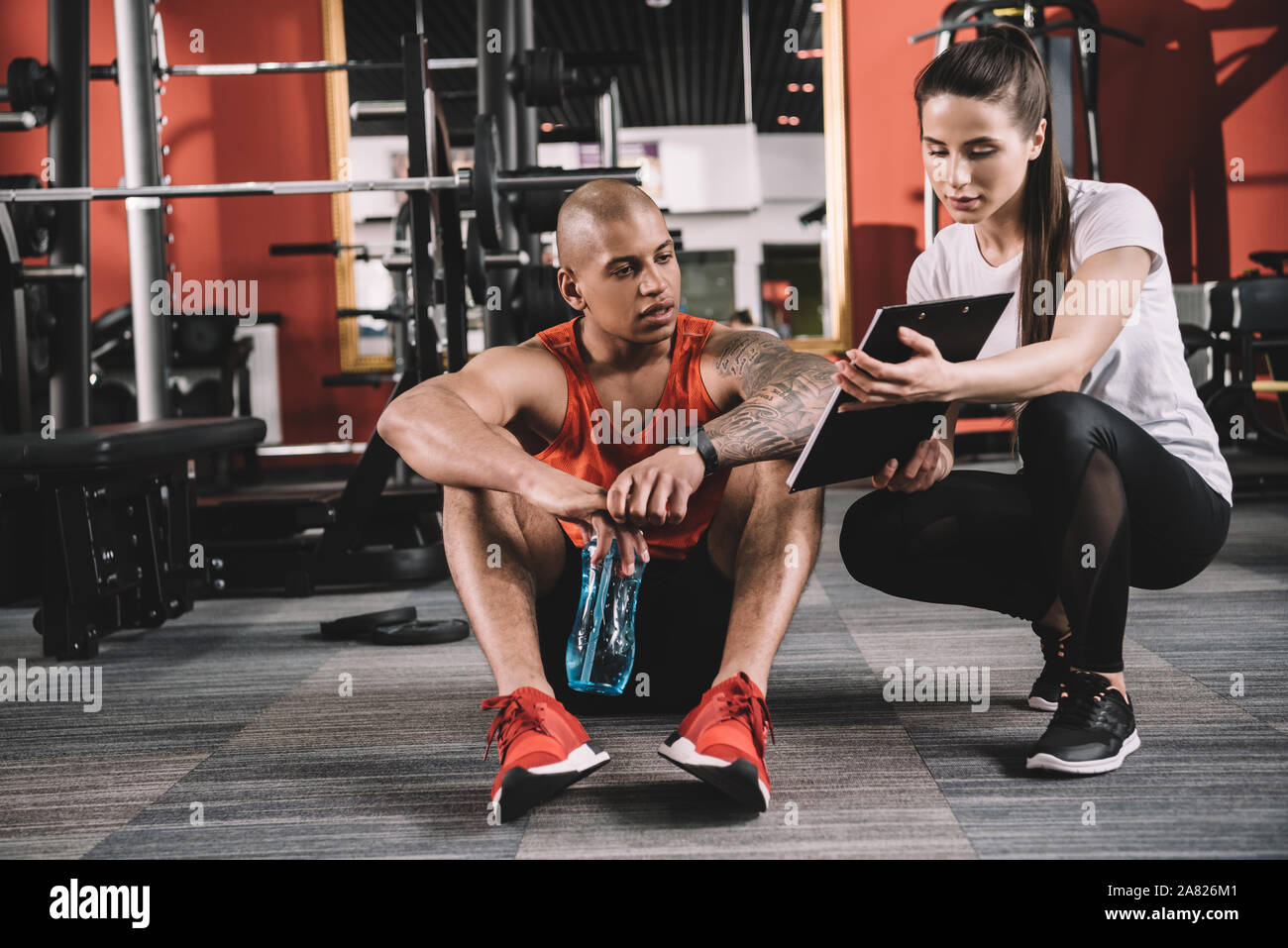 attractive trainer showing clipboard to african american sportsman ...