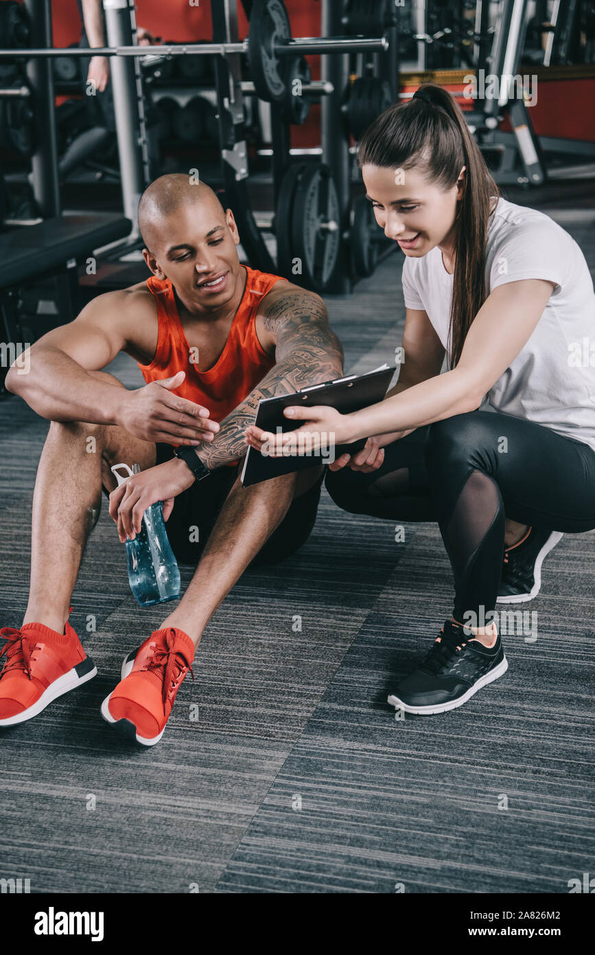 smiling trainer showing clipboard to cheerful african american ...