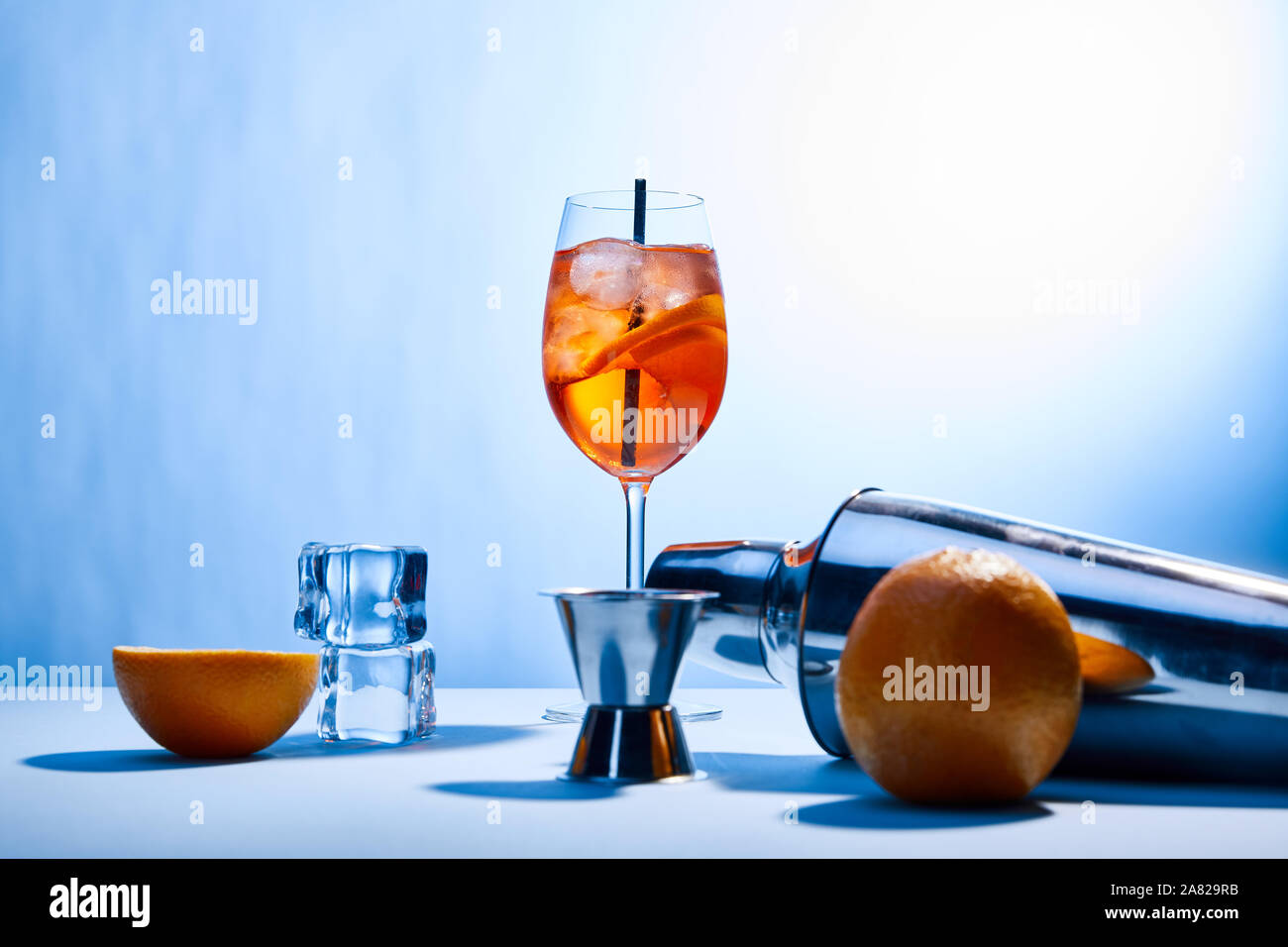 Aperol Spritz, oranges, shaker, ice cubes and measuring cup on blue ...