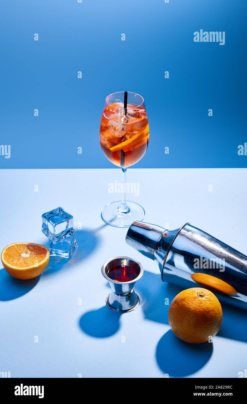 Aperol Spritz, oranges, shaker, ice cubes and measuring cup on blue ...