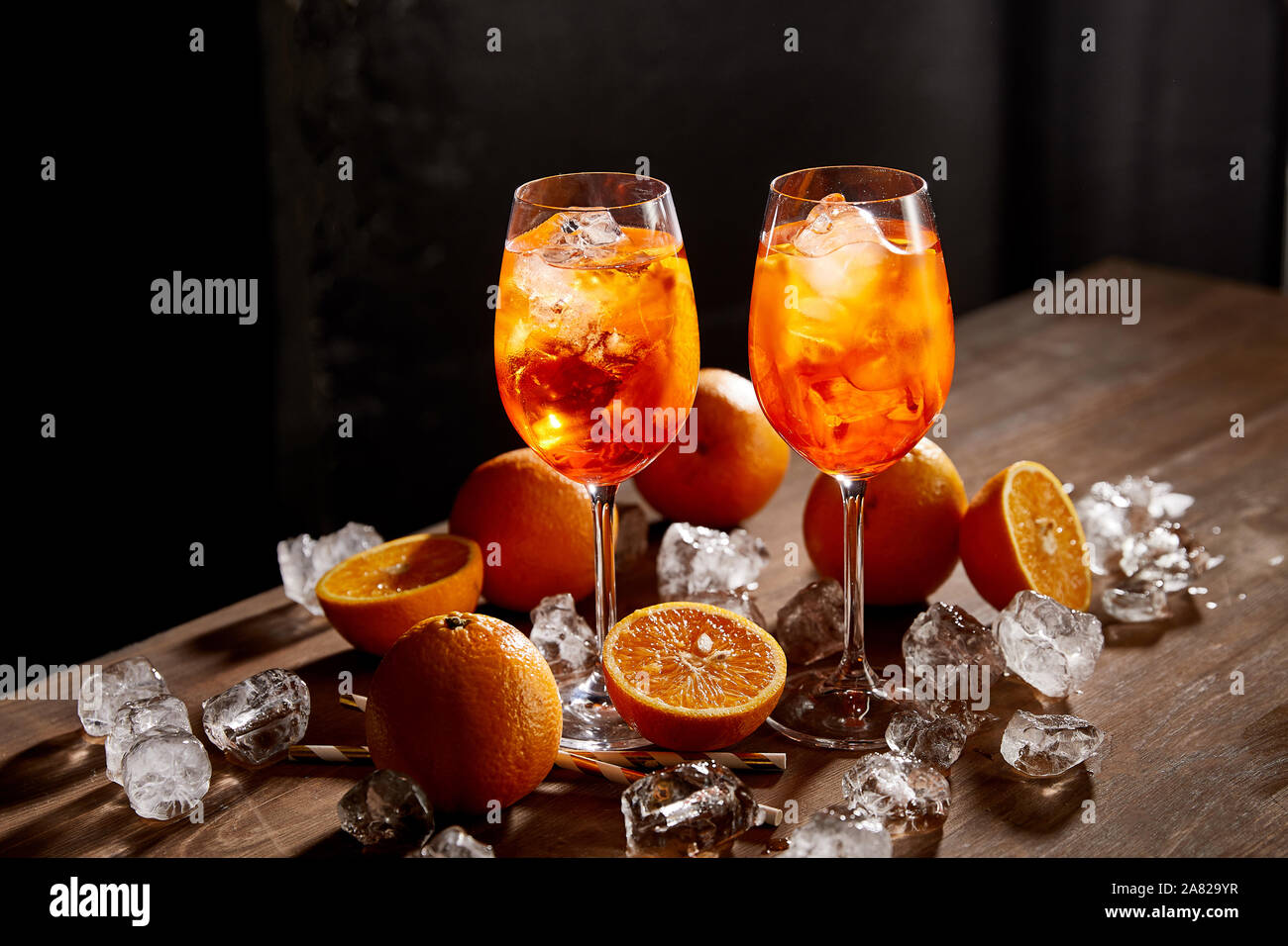Aperol Spritz in glasses, oranges and ice cubes on black background ...