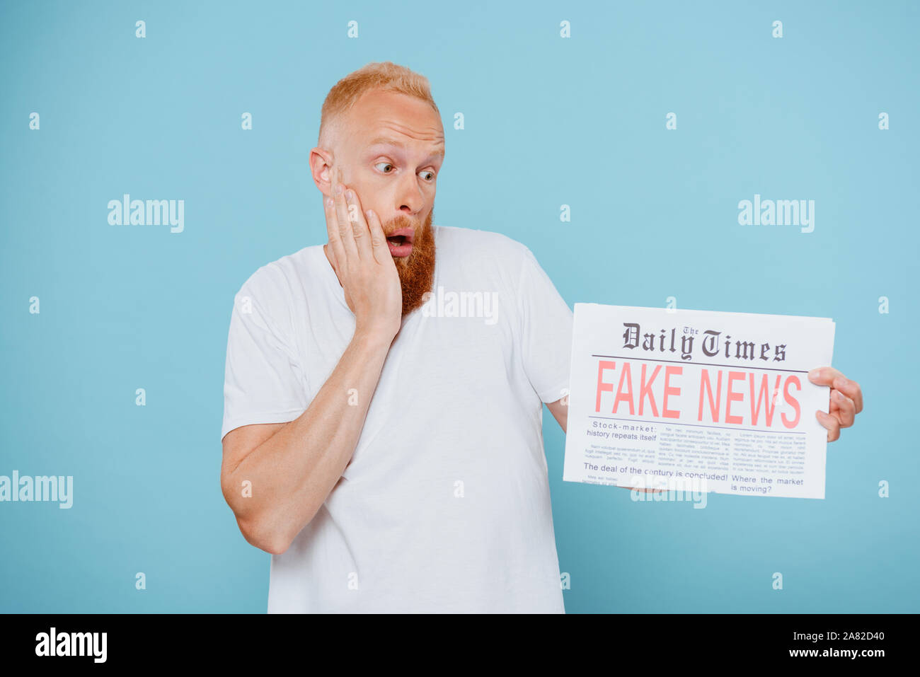 shocked man looking at newspaper with fake news, isolated on blue Stock ...
