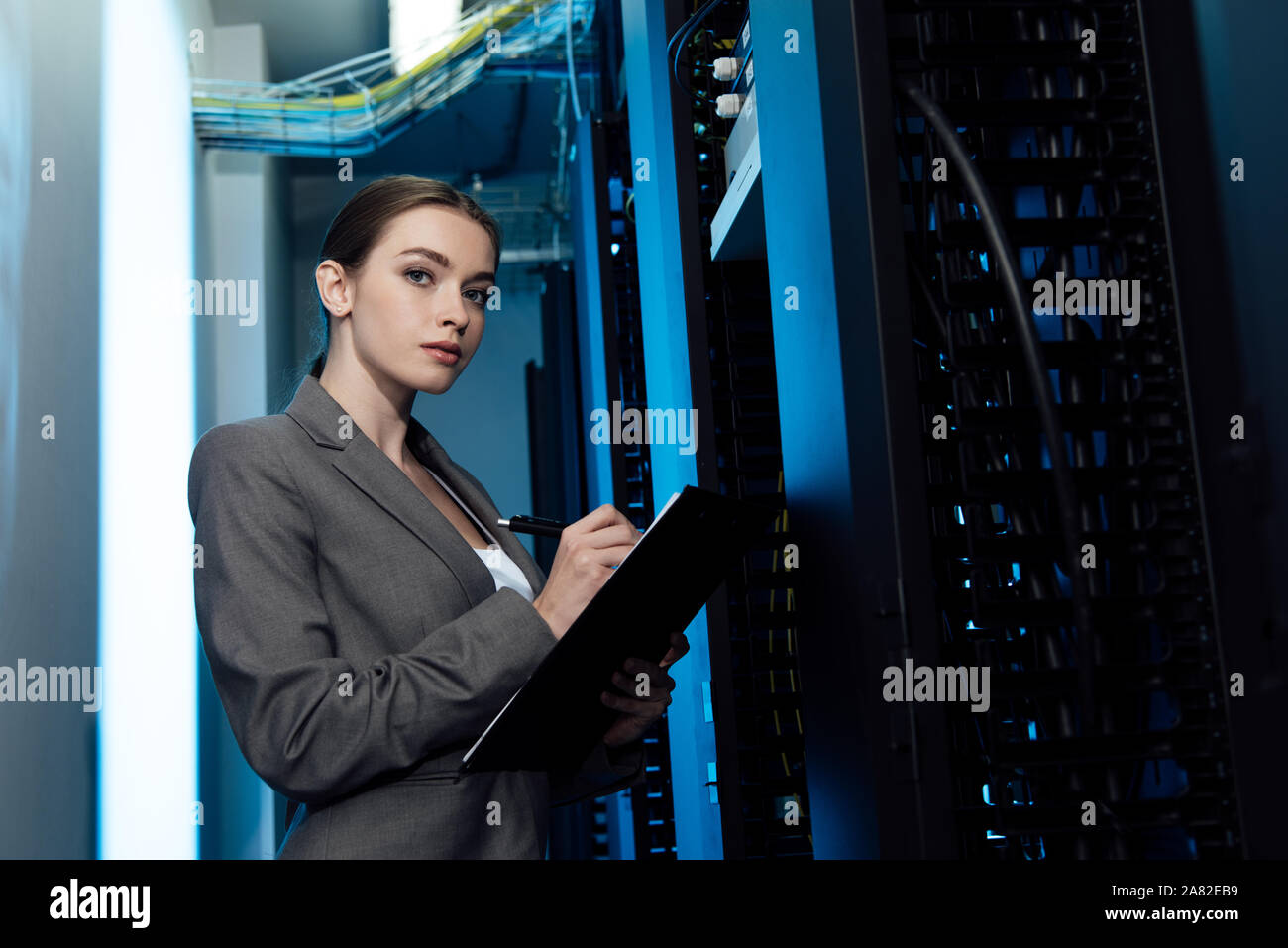 beautiful businesswoman writing while holding clipboard in server room ...