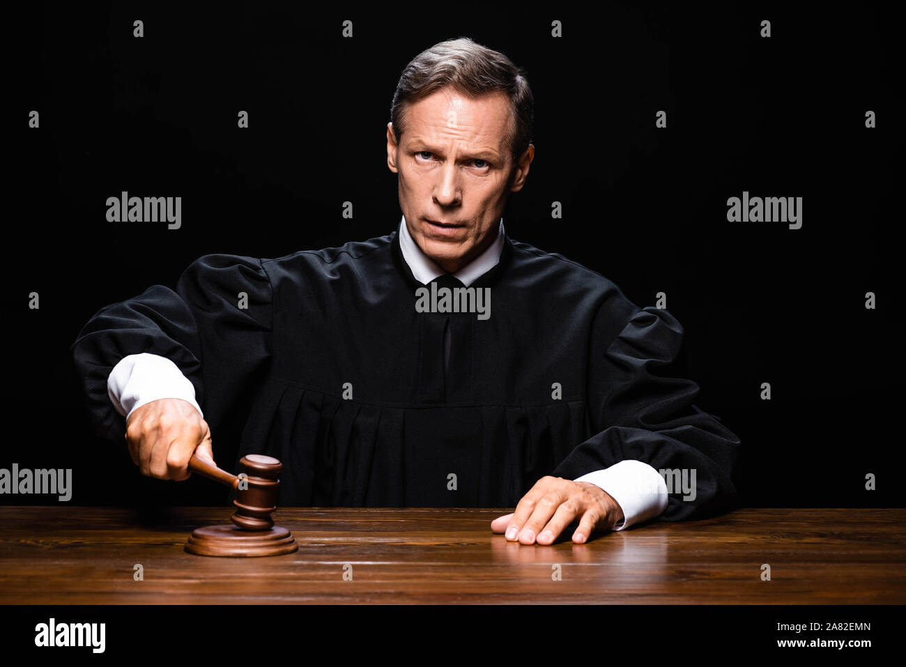 judge in judicial robe sitting at table and hitting with gavel isolated ...