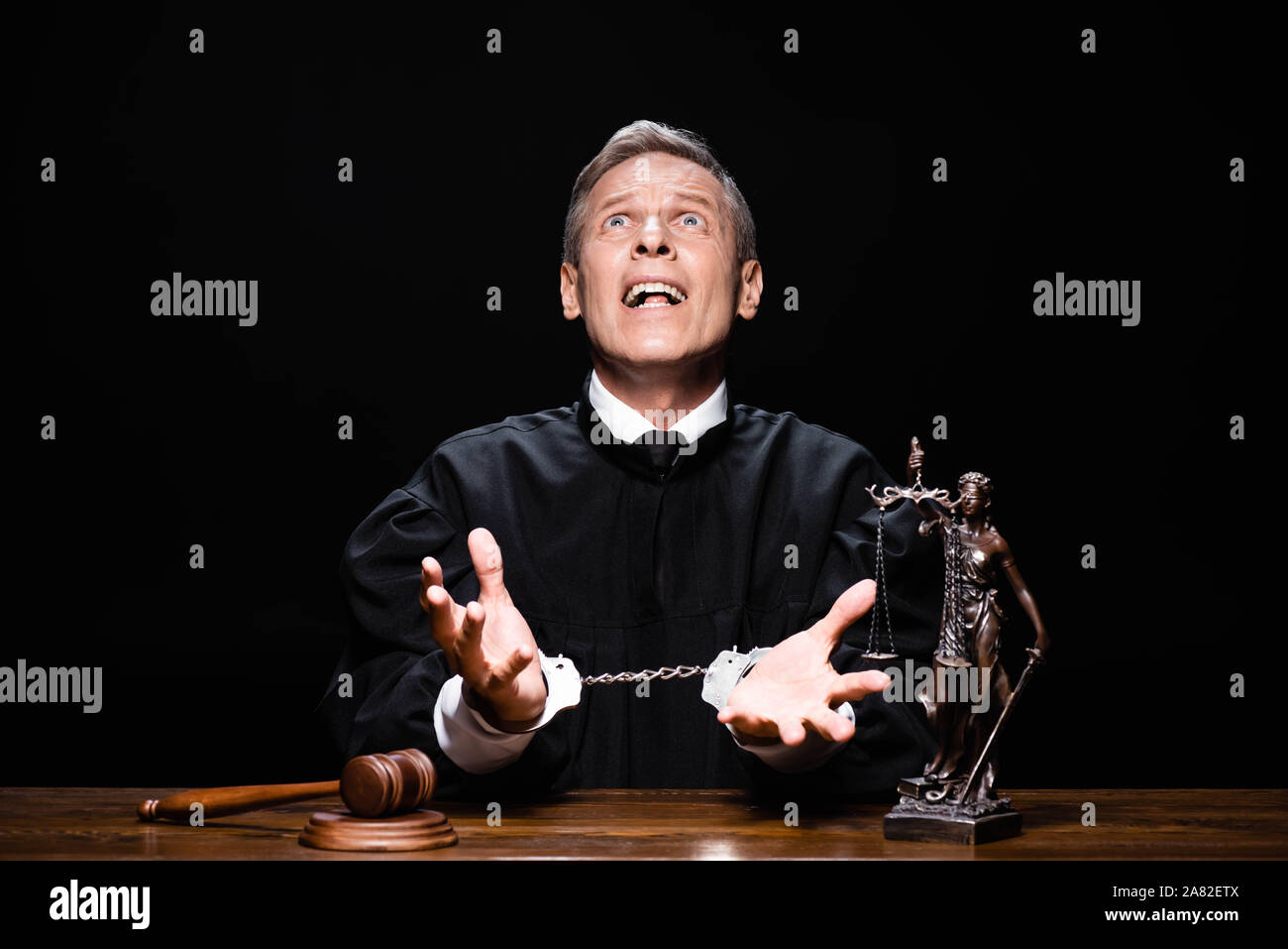 angry judge in judicial robe sitting at table with handcuffs and scream ...