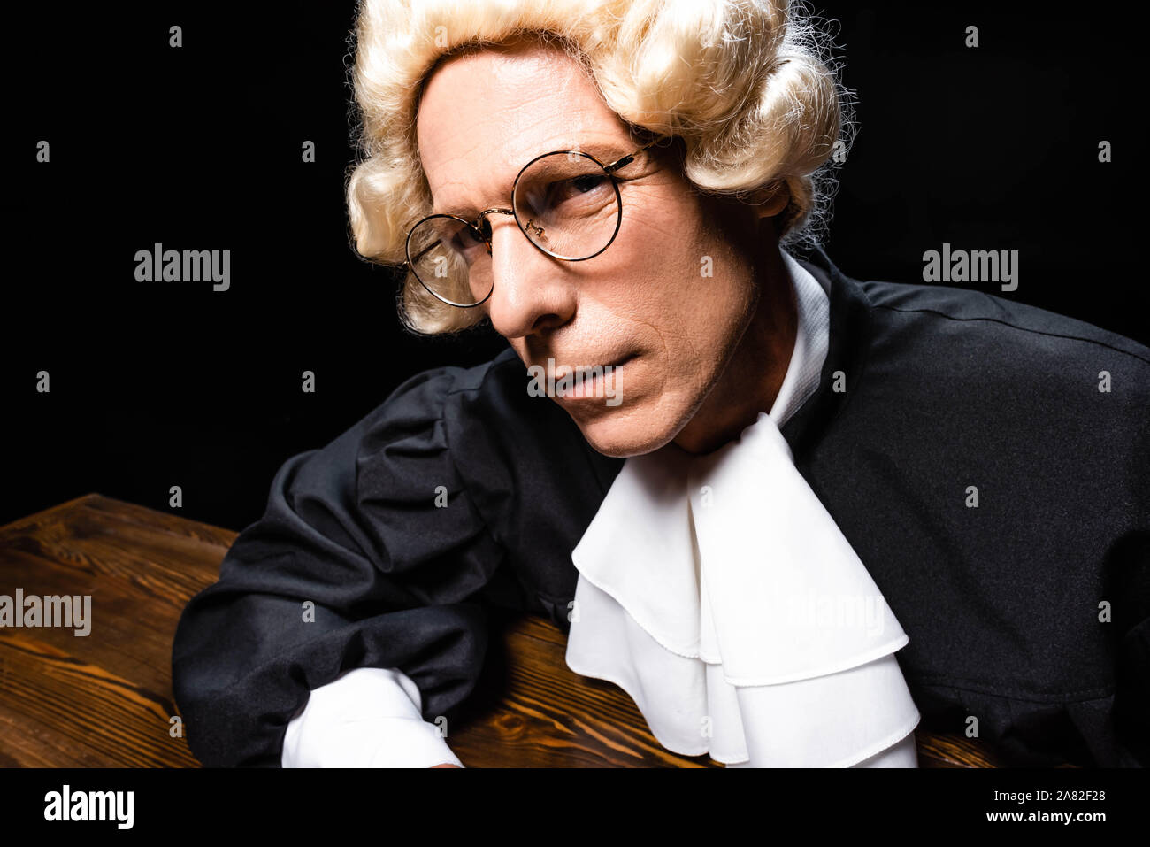 judge in judicial robe and wig sitting at table and looking at camera ...