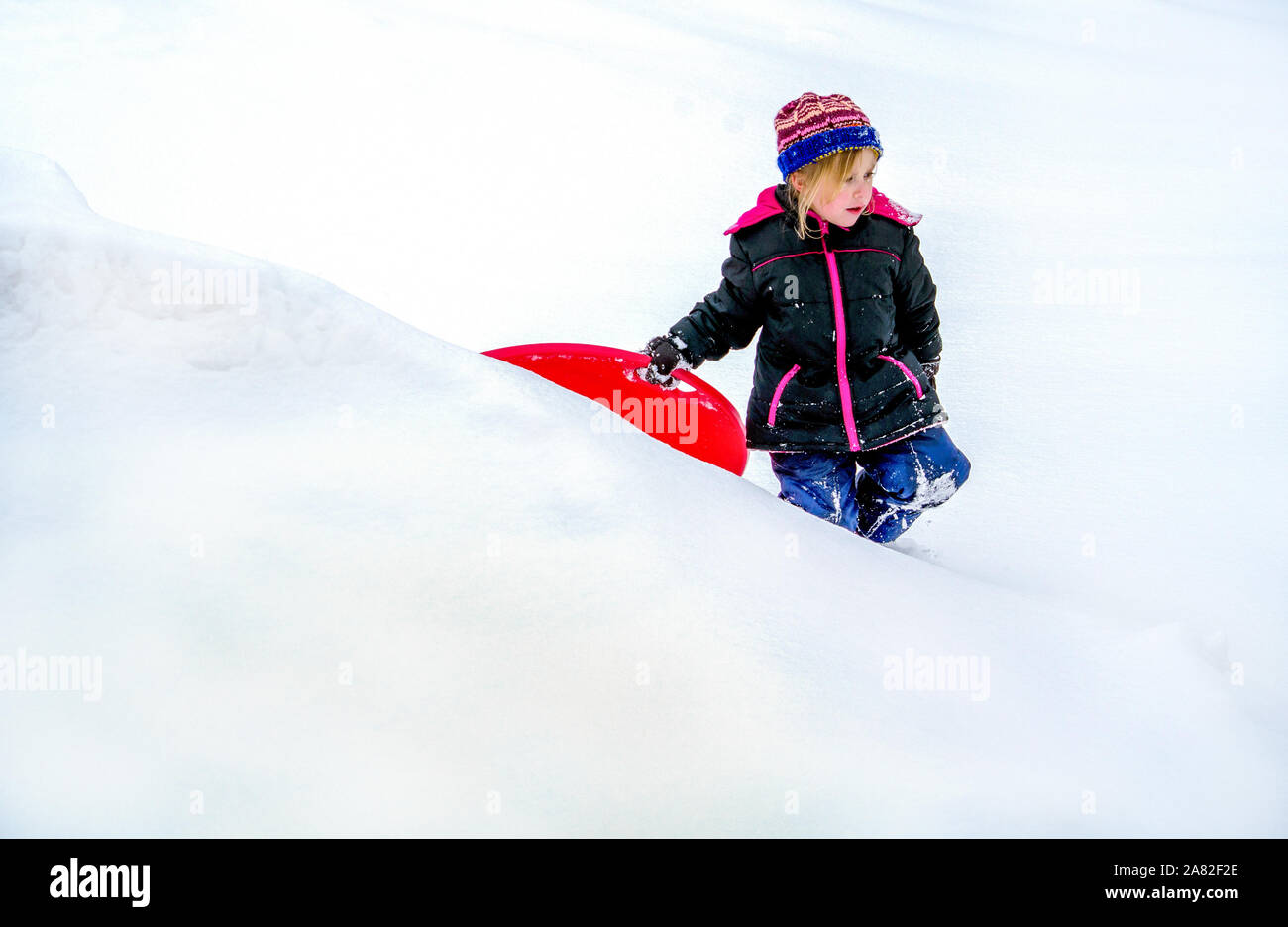 A adorable little girl walks through the snow with her red sled Stock ...