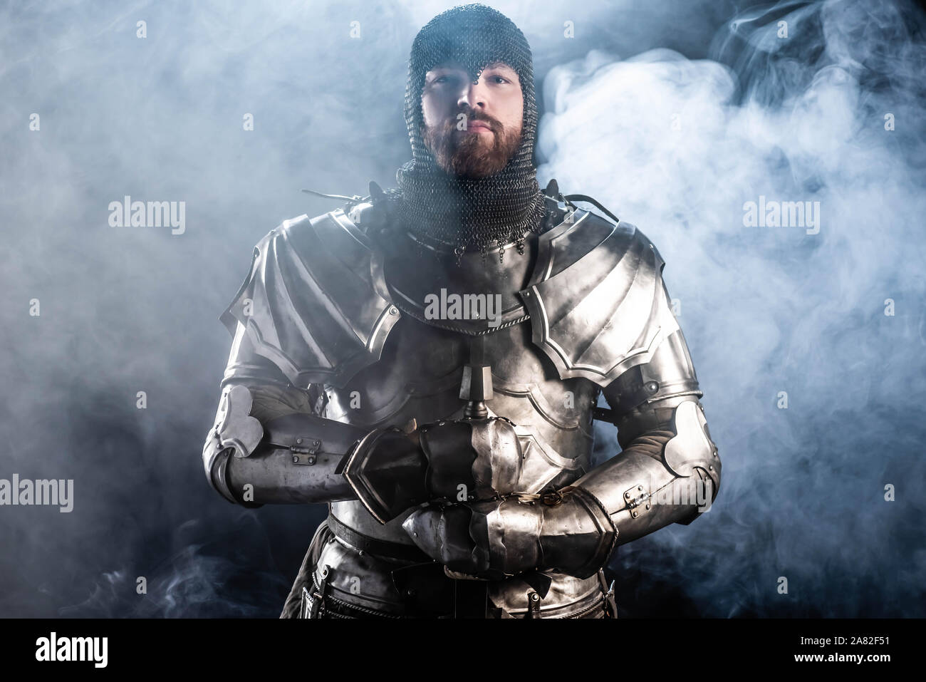 handsome knight in armor looking at camera and holding sword on black ...