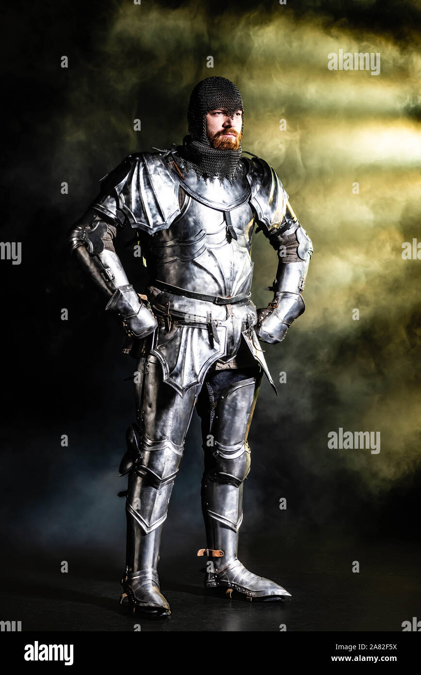 handsome knight in armor looking away with hands on hips on black ...