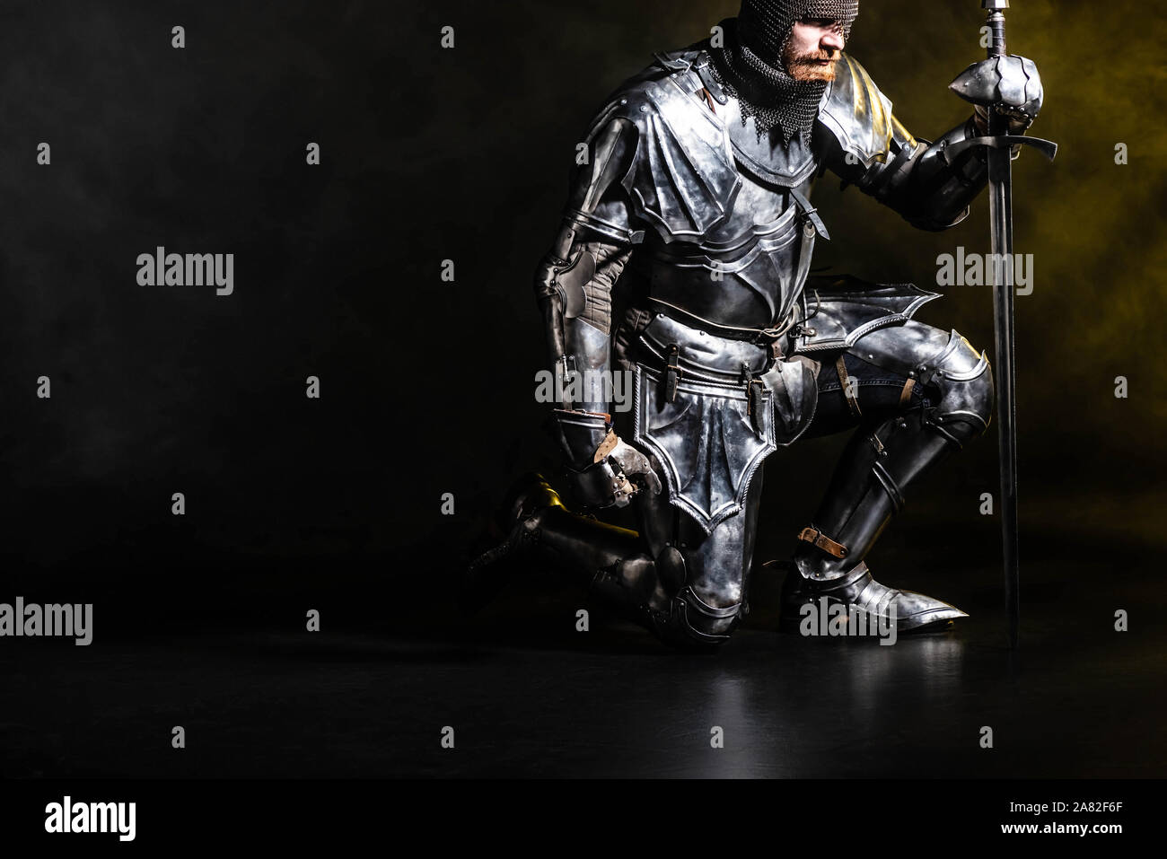 handsome knight in armor holding sword and bend knee on black ...