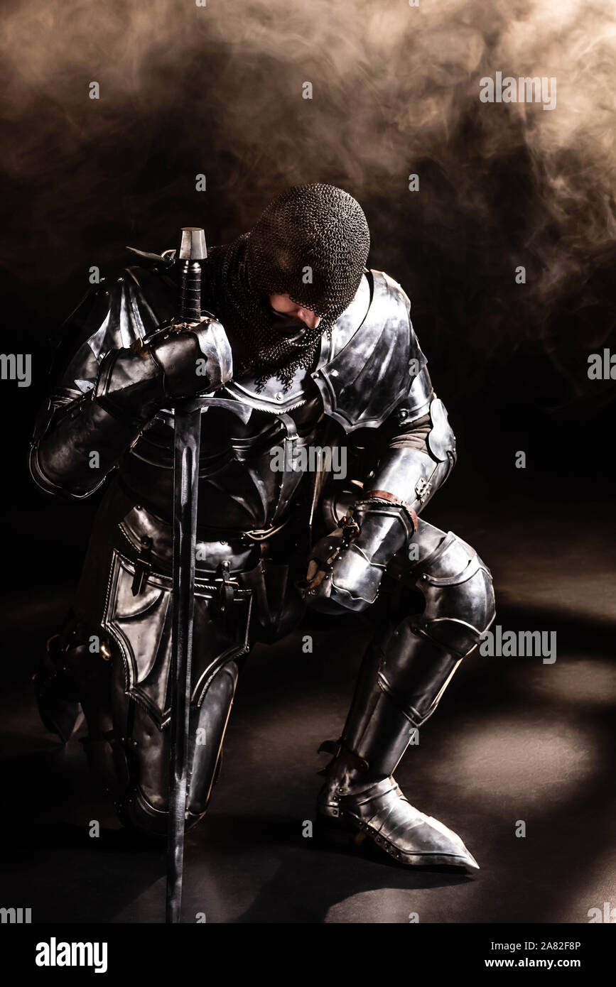 handsome knight in armor holding sword and bend knee on black ...