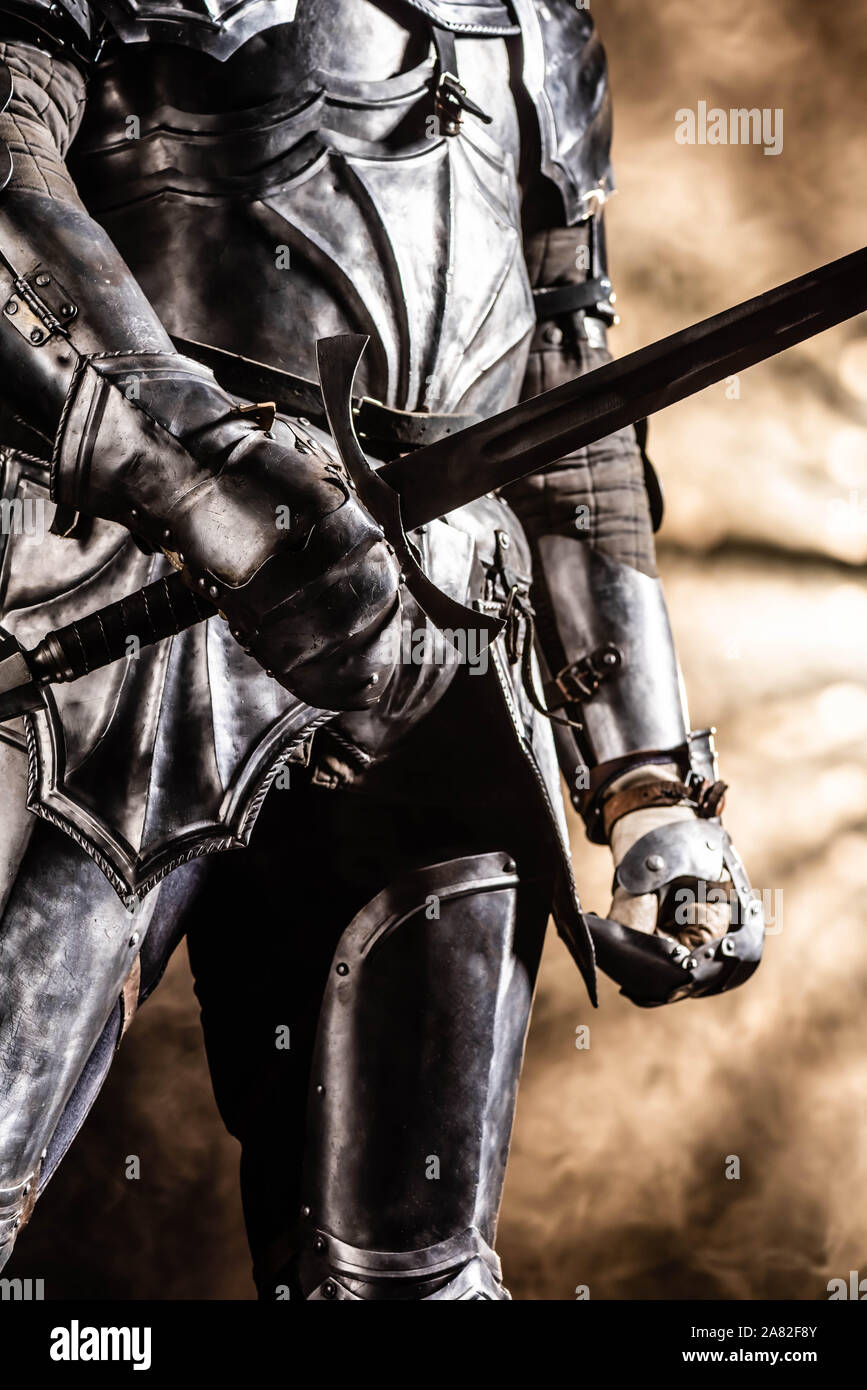 cropped view of knight in armor holding sword on black background Stock ...
