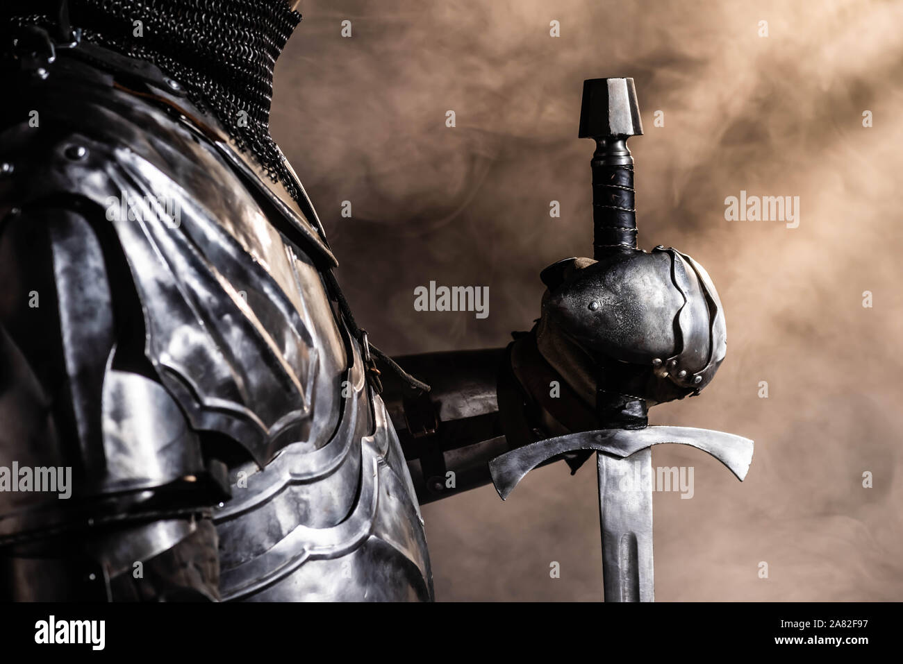 cropped view of knight in armor holding sword on black background Stock ...