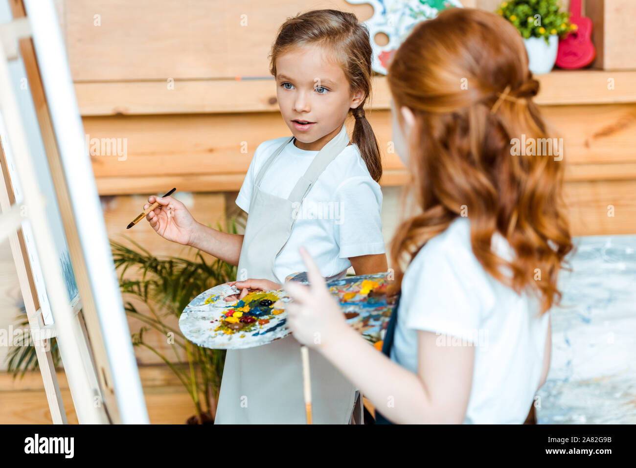 selective focus of cute kid looking at easel near redhead child in art school Stock Photo - Alamy