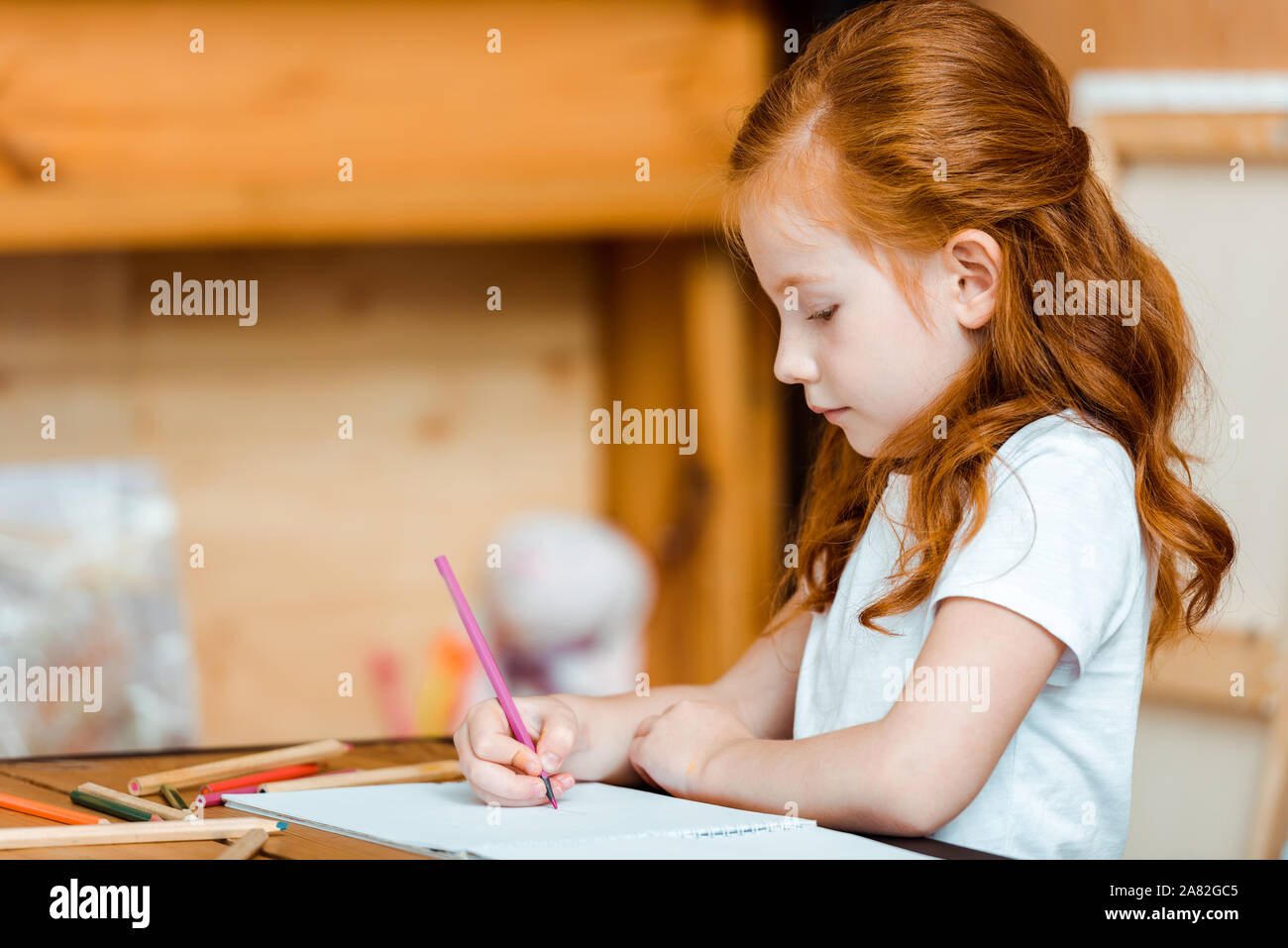 cute redhead child holding color pencil while drawing on paper Stock Photo - Alamy