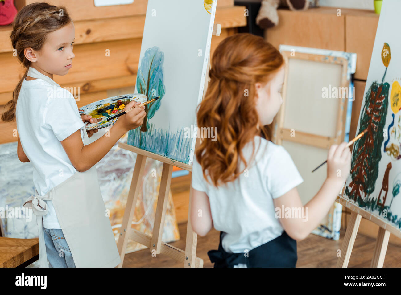 selective focus of cute kid looking at child painting on canvas in art ...