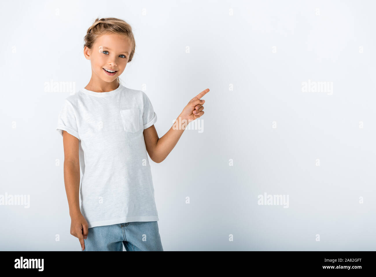 cheerful kid looking at camera and pointing with finger on white Stock ...