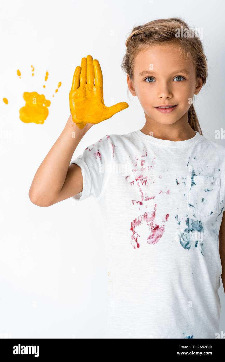 cute kid showing yellow paint on hand near yellow hand print on white ...