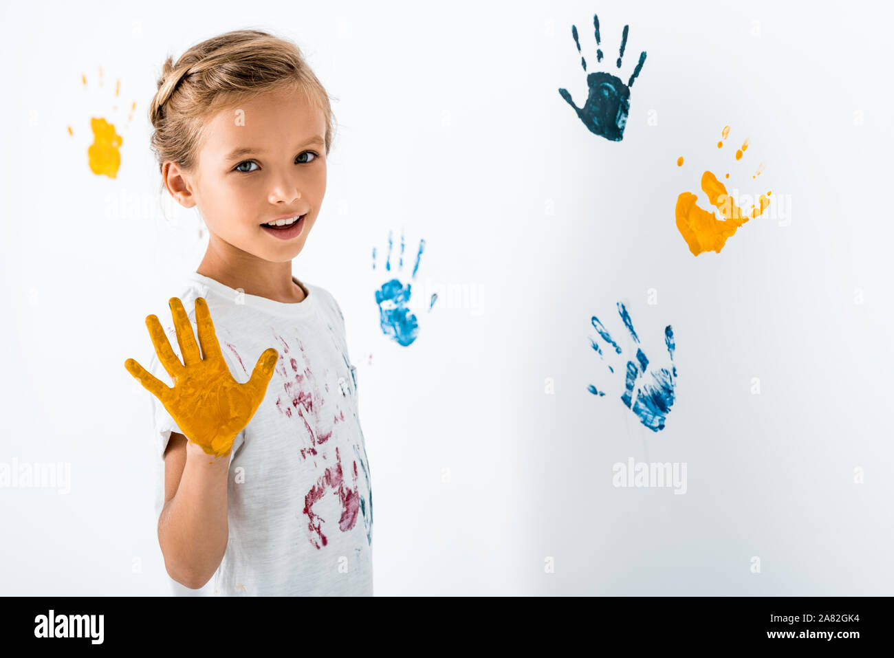 happy kid with yellow paint on hand near hand prints on white Stock ...