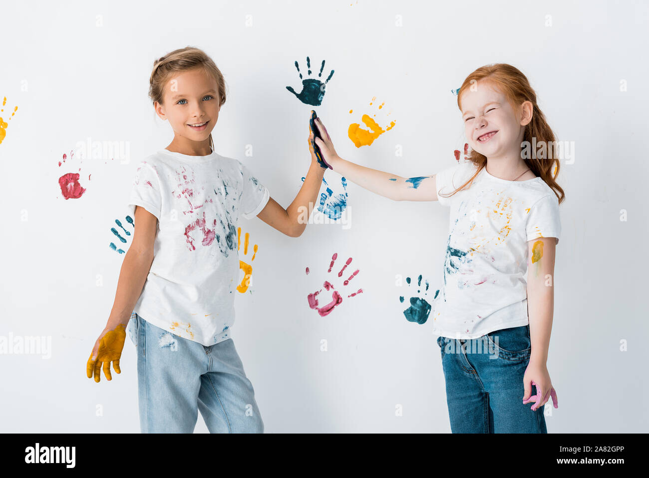 cheerful kids giving high five near hand prints on white Stock Photo ...