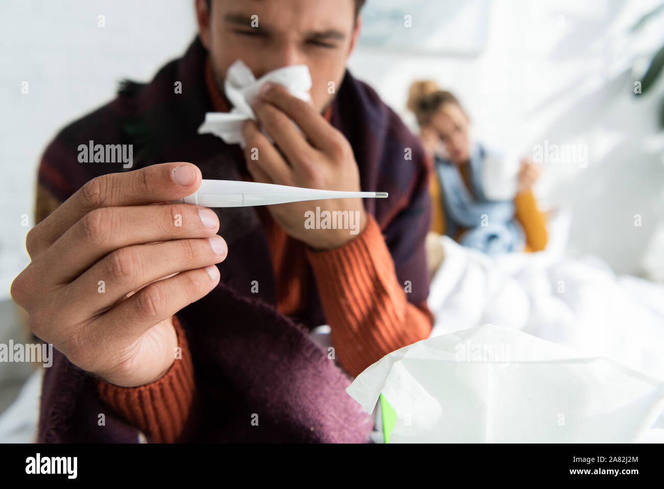 selective focus of sick man with fever holding thermometer and napkin ...