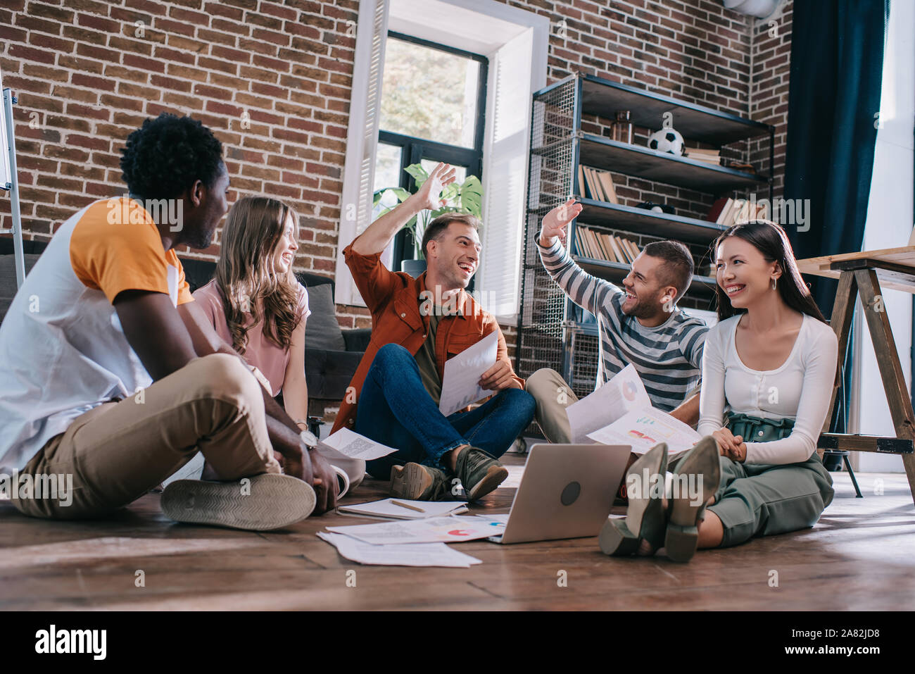 happy businessmen giving high five while sitting on floor near young ...