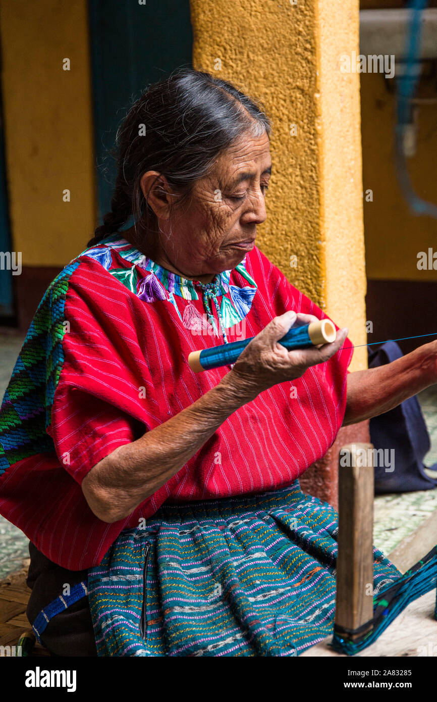 An older Mayan woman in traditional dress winds thread in preparation ...