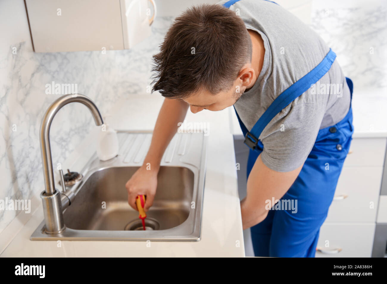 Plumber installing sink in kitchen Stock Photo - Alamy