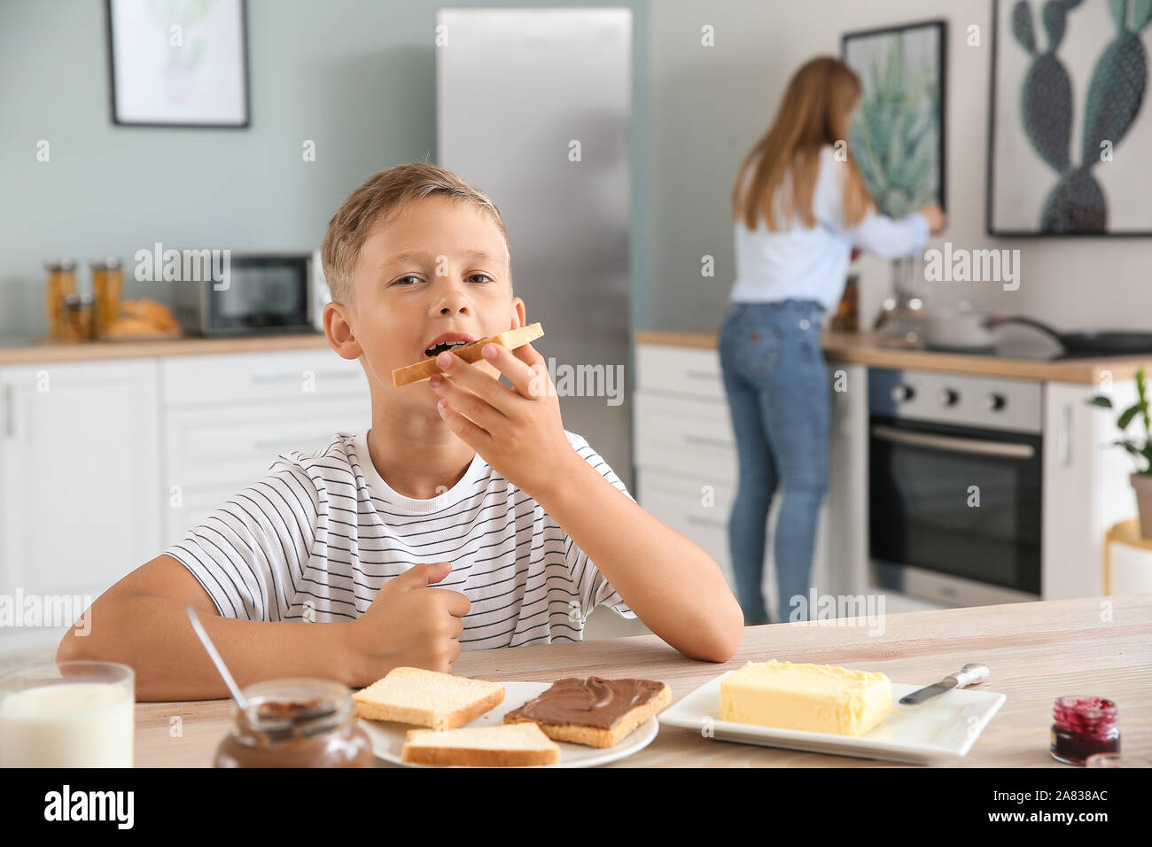 Funny little boy eating tasty toasts with chocolate spreading in ...