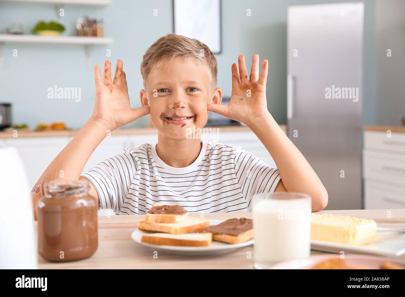 Funny little boy eating tasty toasts with chocolate spreading in ...