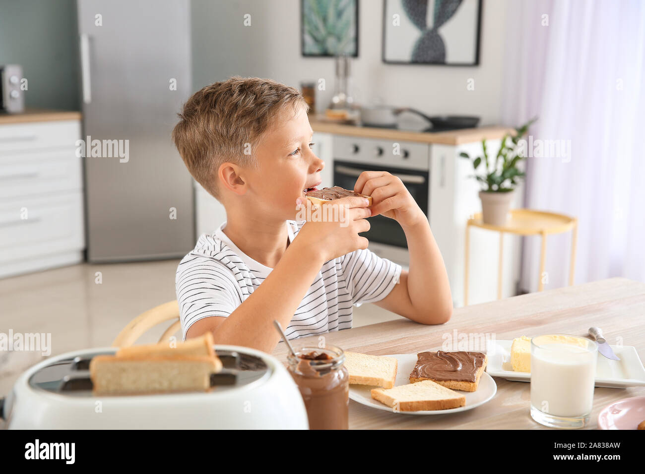 Funny little boy eating tasty toasts with chocolate spreading in ...