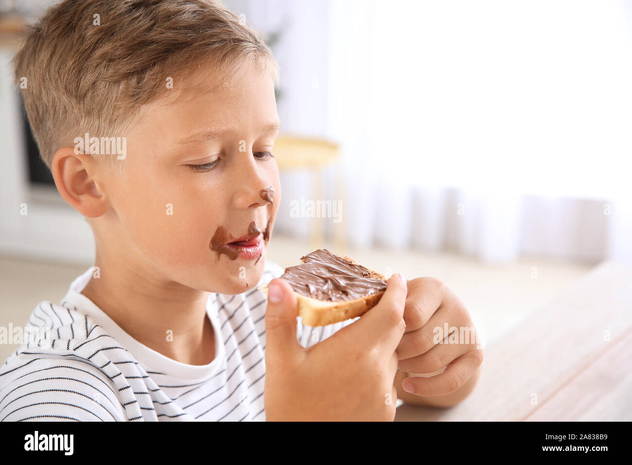 Funny little boy eating tasty toasts with chocolate spreading in ...