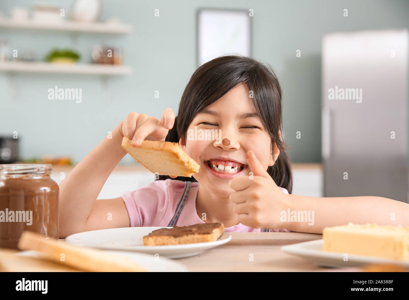 Funny little girl eating tasty toasts with chocolate spreading in ...