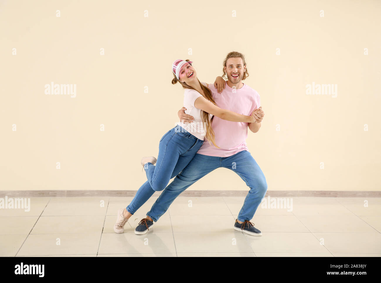 Cool young couple dancing against light wall Stock Photo - Alamy