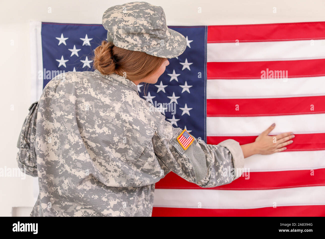Young female soldier hanging USA flag on wall in headquarters building ...