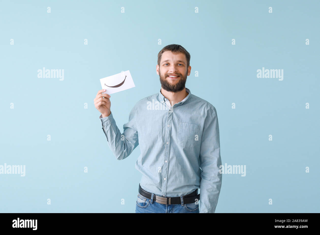 Happy man holding sheet of paper with drawn smile on color background ...