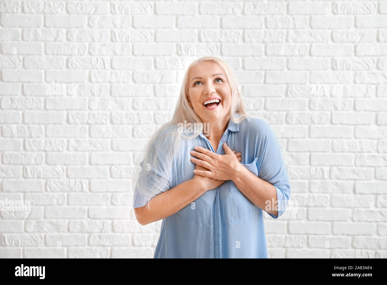 Flattered mature woman against white brick wall Stock Photo - Alamy