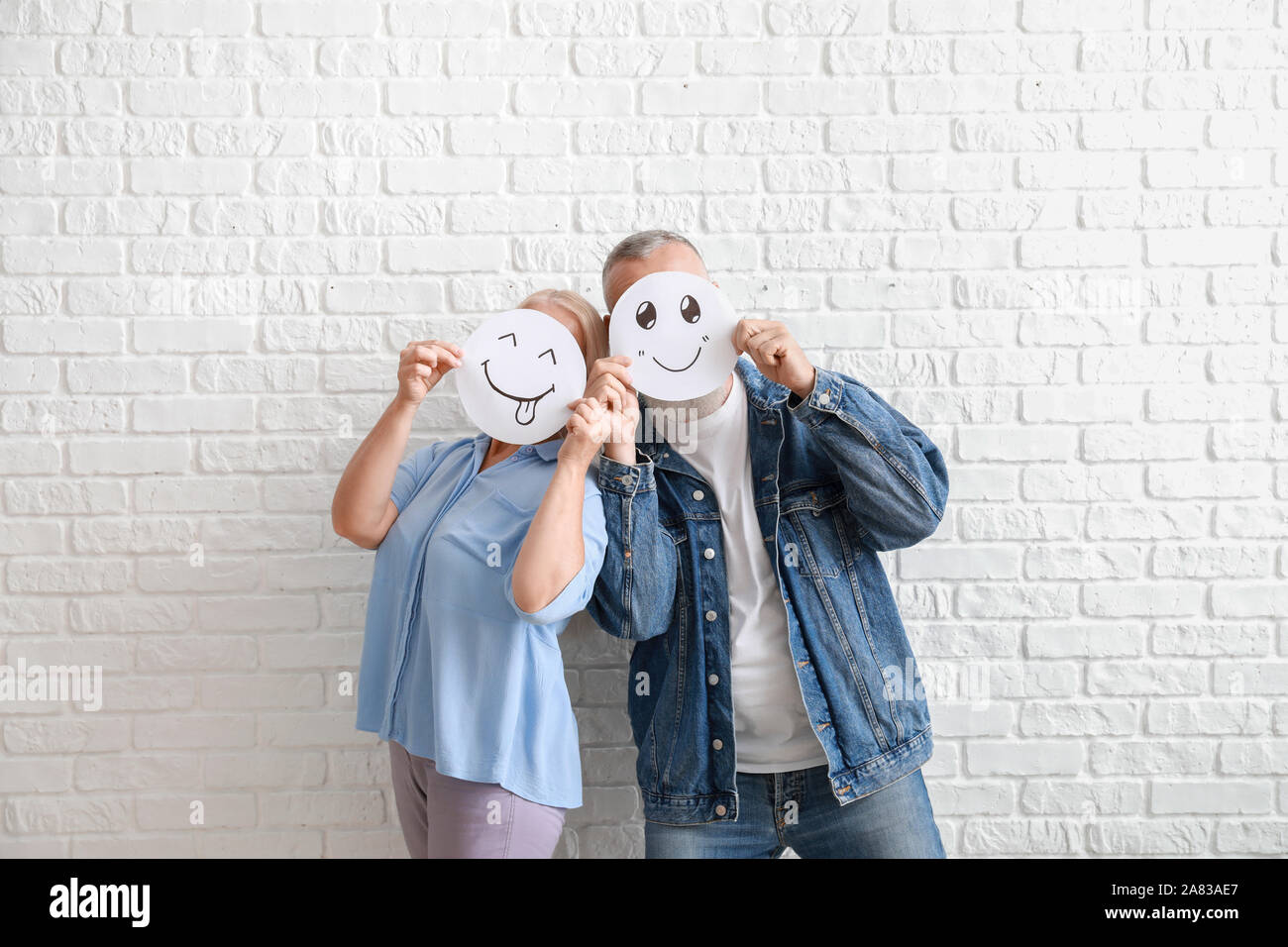 Mature couple hiding faces behind emoticons against white brick wall ...