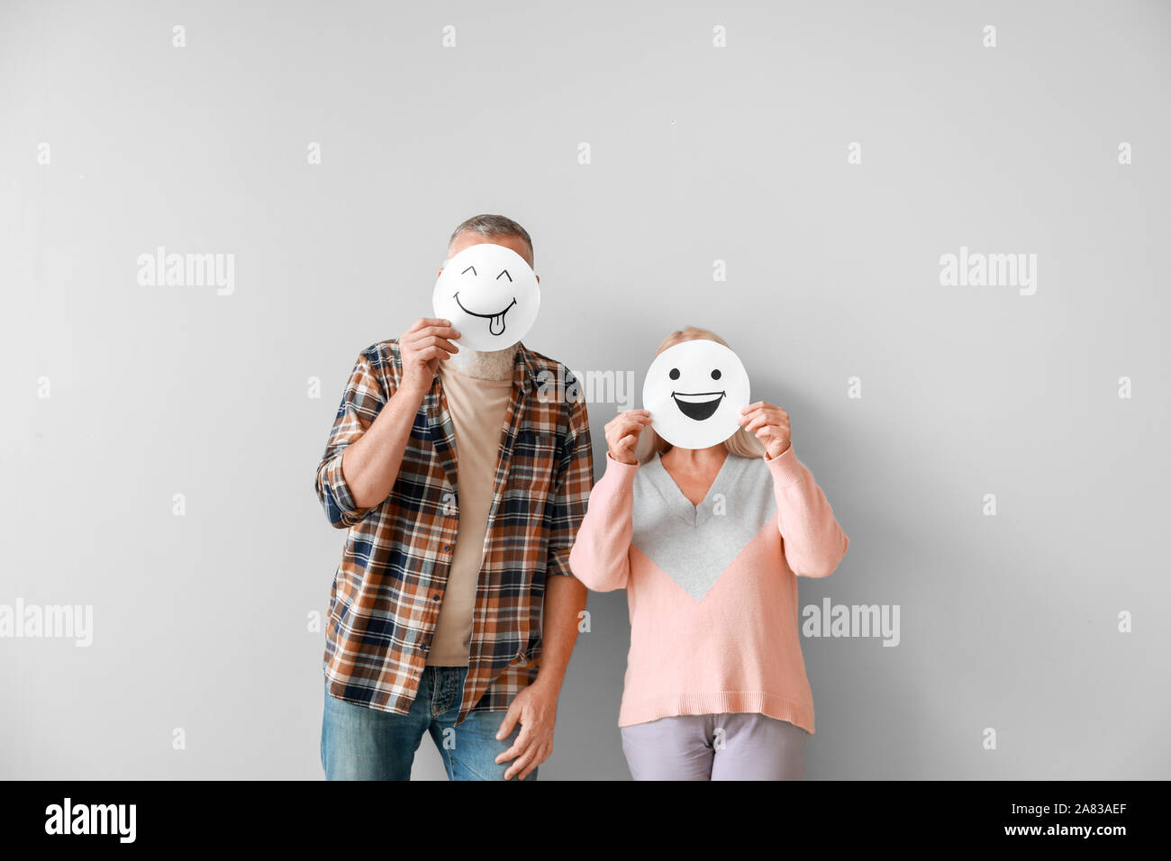 Mature couple hiding faces behind emoticons against light background ...