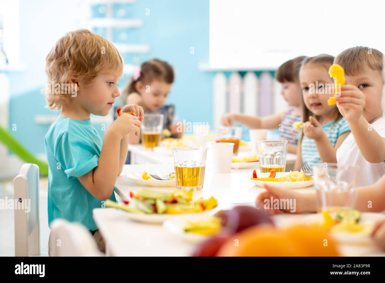 Group of children have dinner. Kids eating healthy food in kindergarten ...