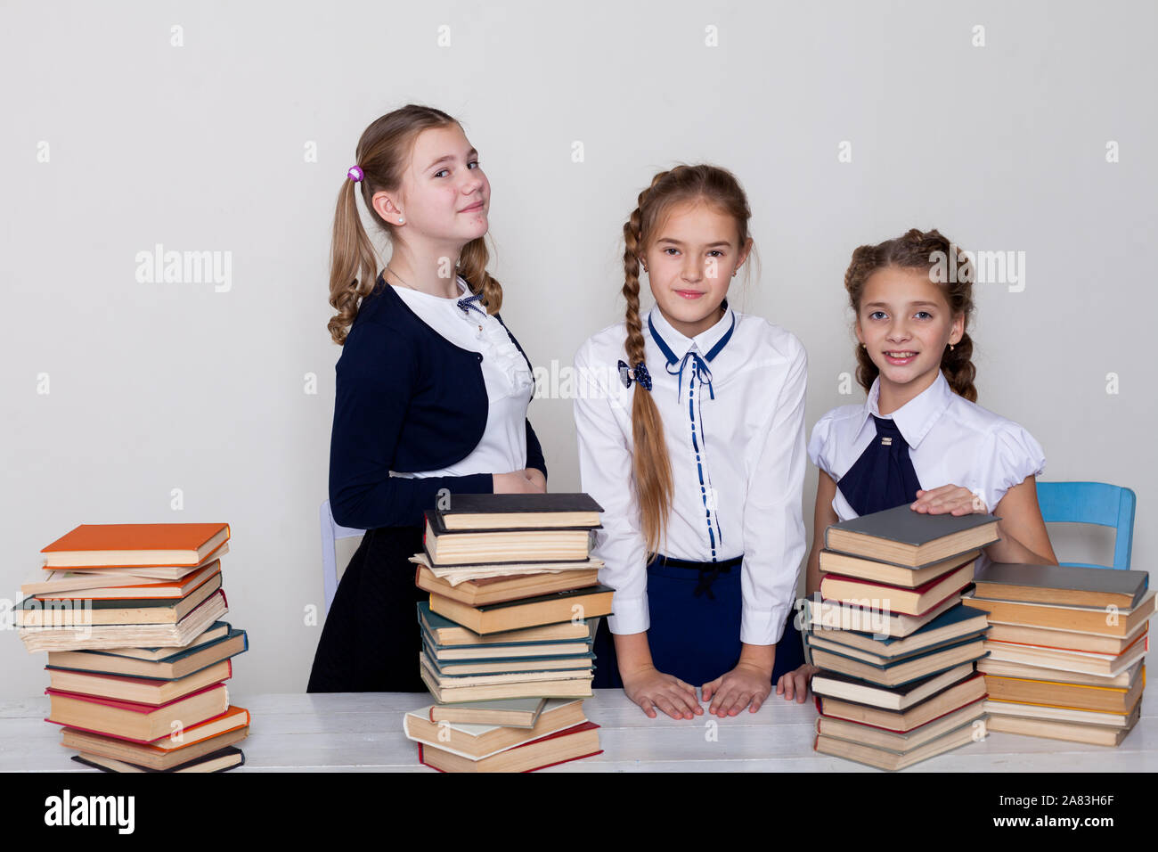 three schoolgirl girls with books in the library in class at the desk ...