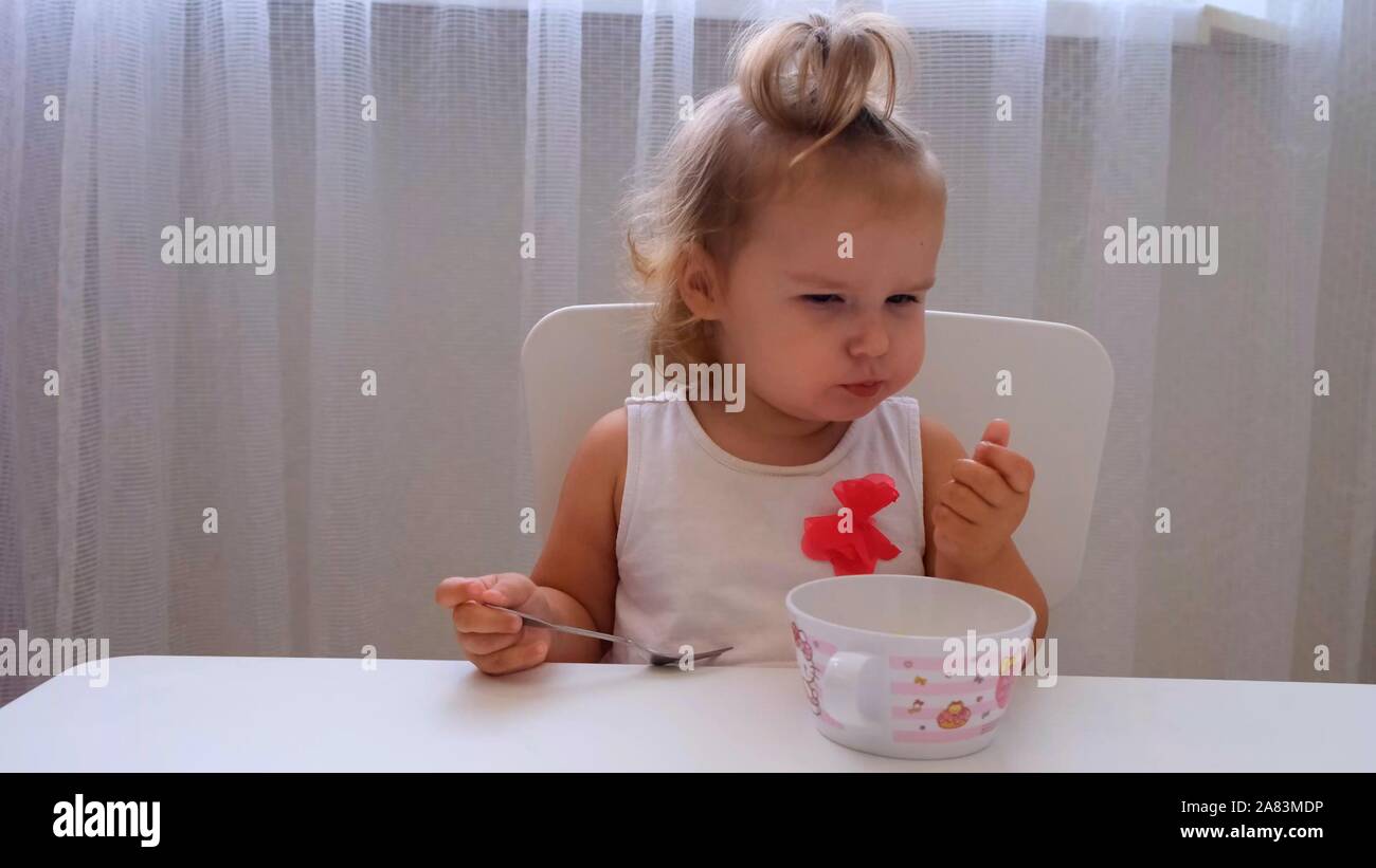 Infant girl eating baby food at a small childrens table on a white ...