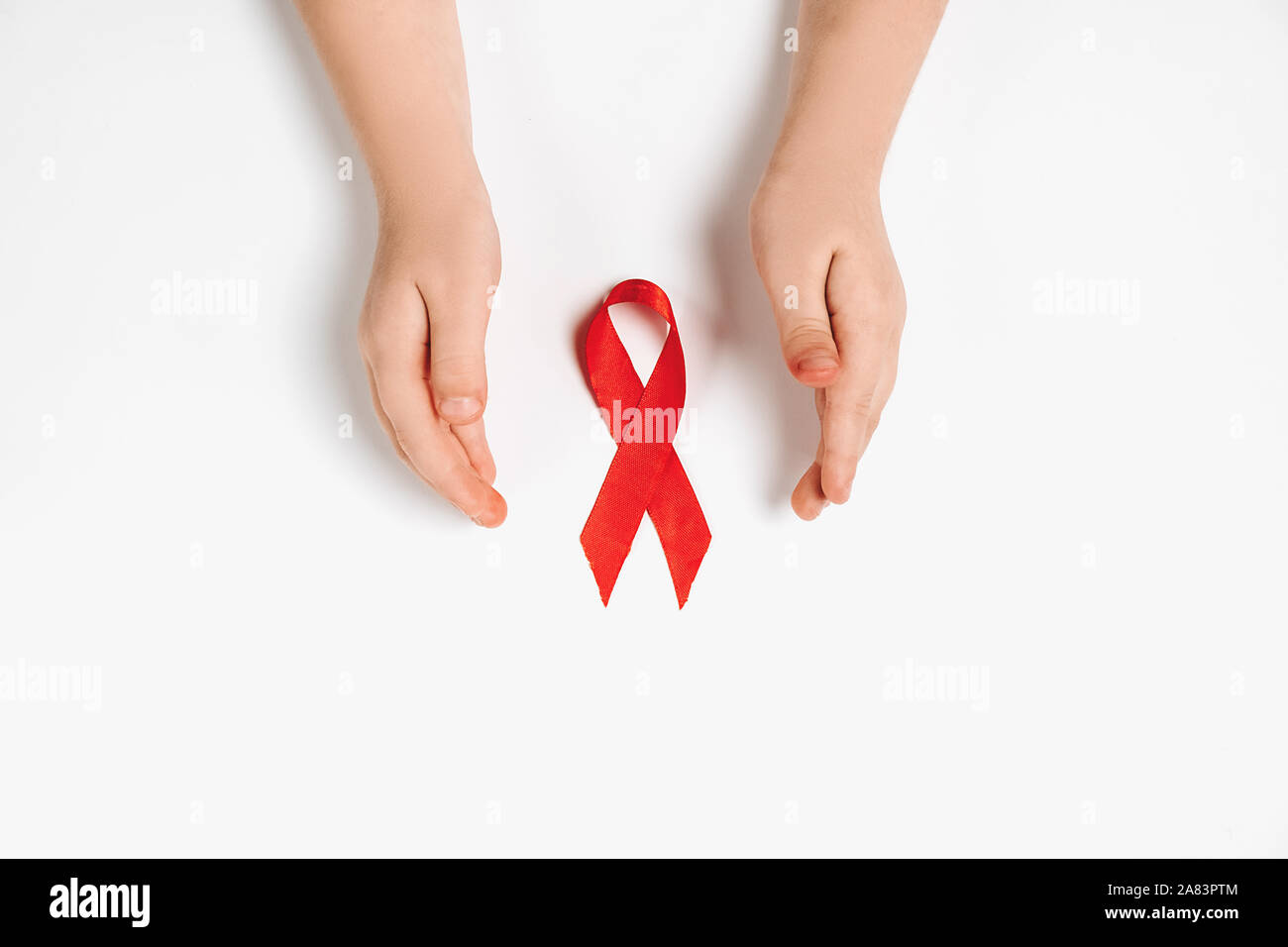 Top view on child's hands holding red ribbon on white background, HIV awareness concept, world ...