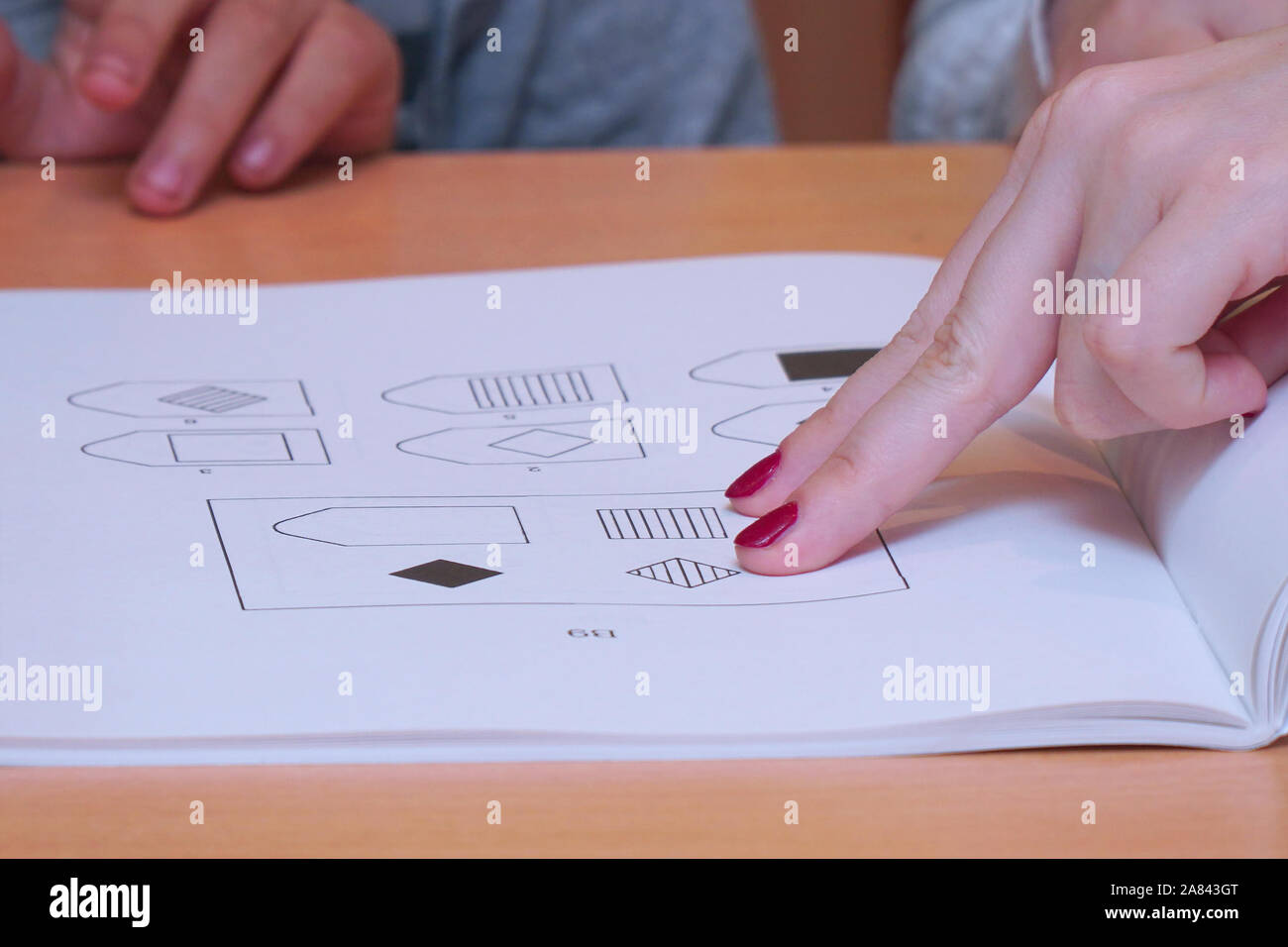 The teacher points a finger at the shapes in the geometry textbook ...